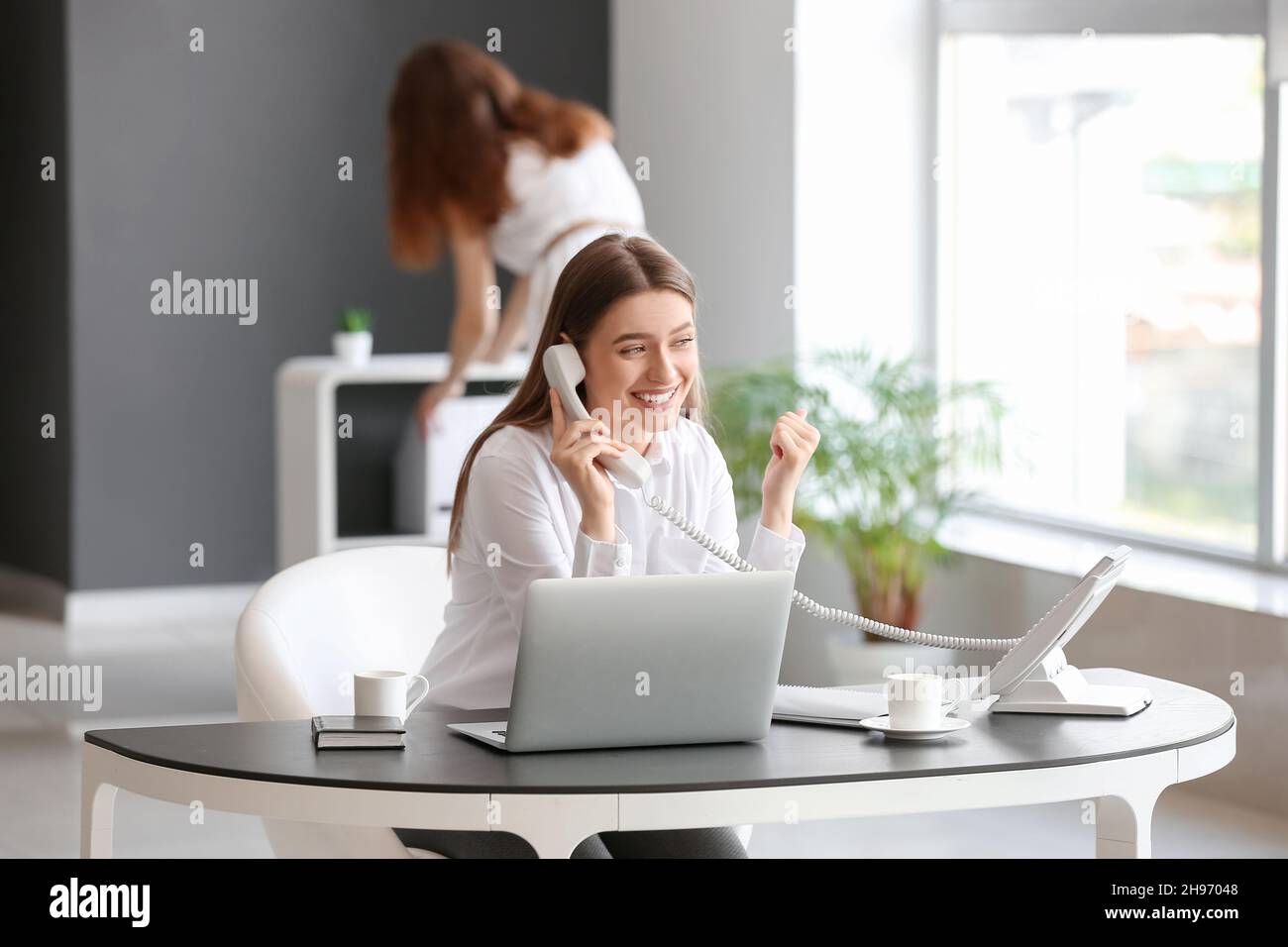 Young woman gossiping while talking by phone in office Stock Photo - Alamy