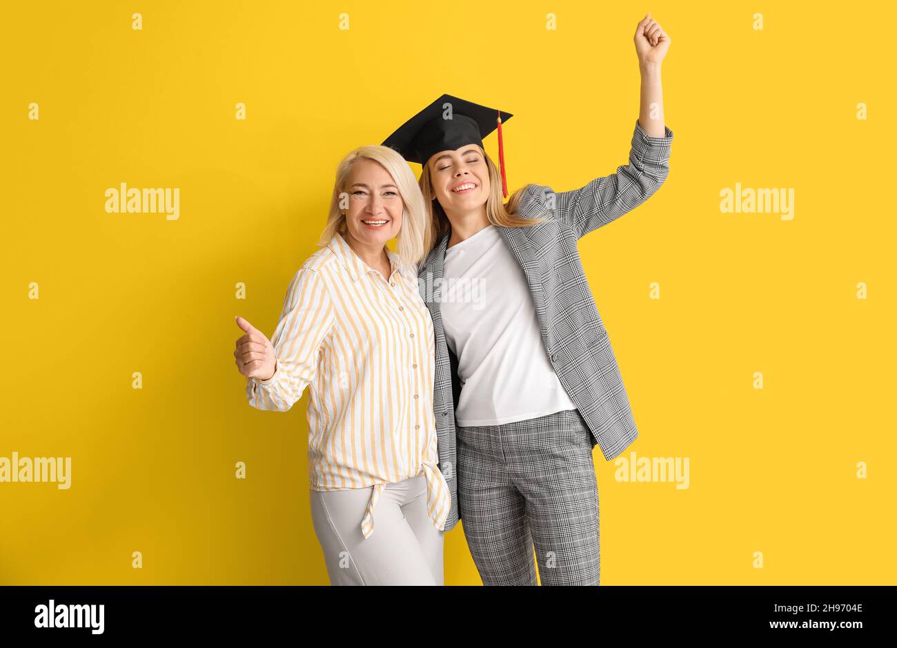 Happy female graduation student with her mother on color background ...