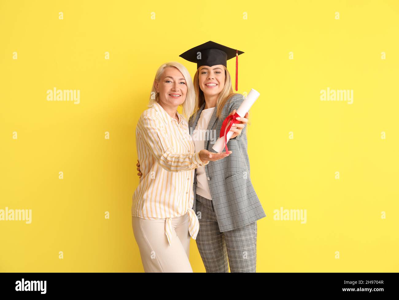 Happy female graduation student with her mother on color background ...