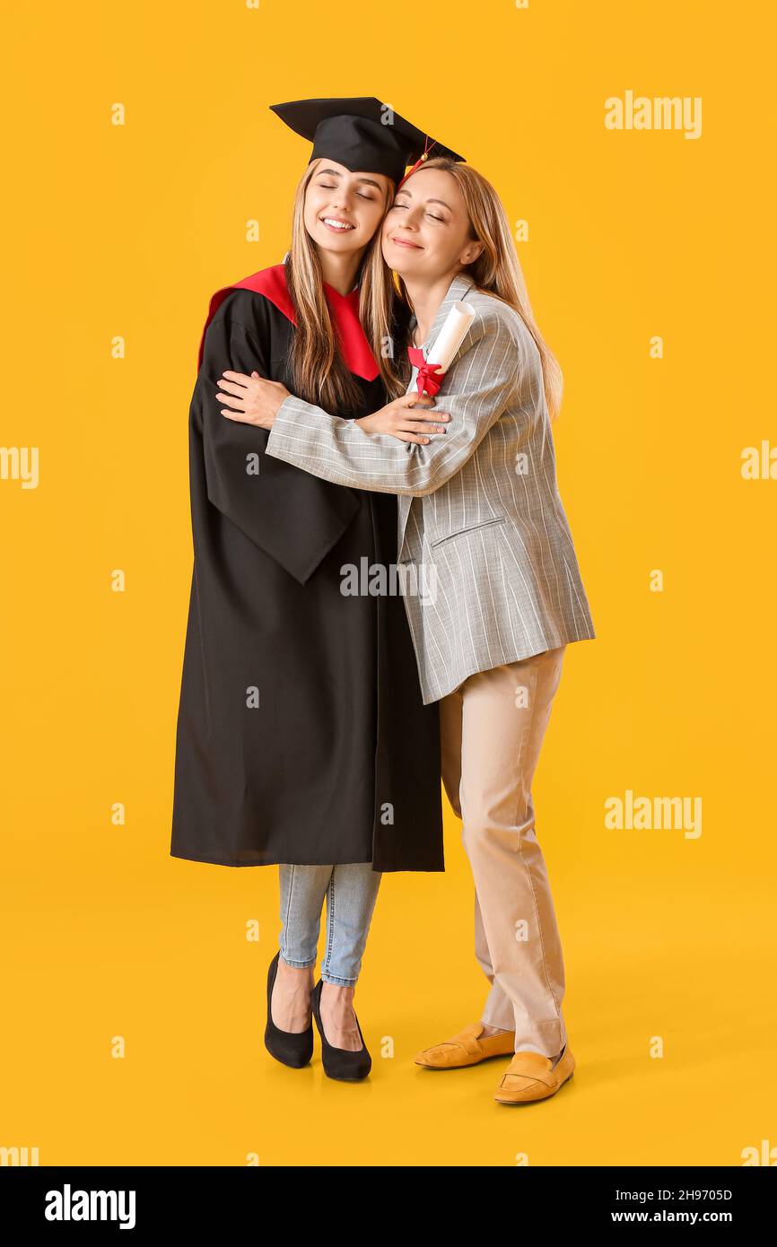 Happy female graduation student with her mother on color background ...