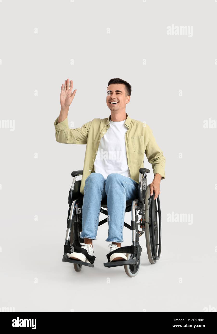 Young man in wheelchair waving hand on light background Stock Photo - Alamy