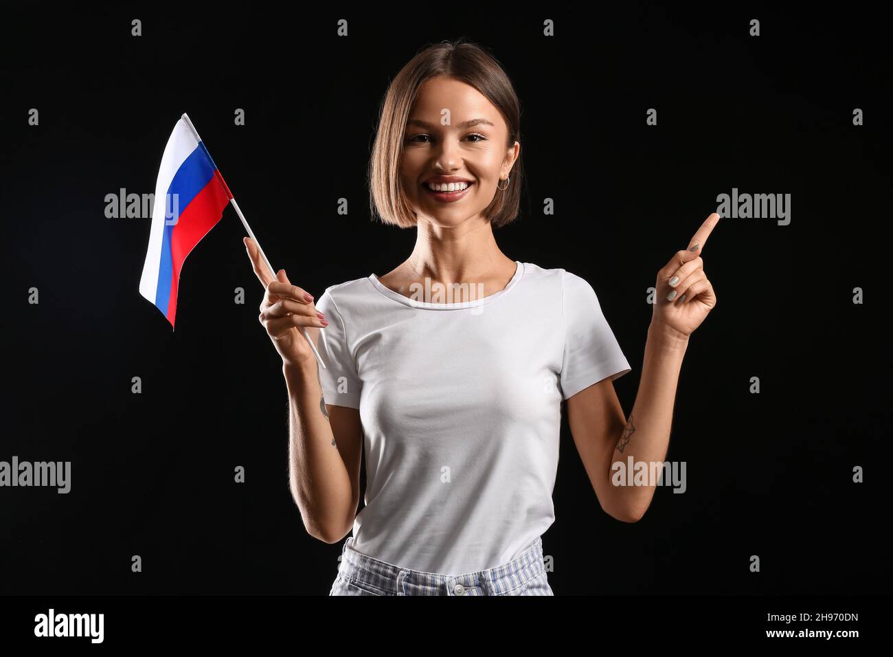 Beautiful young woman with flag of Russia pointing at something on dark ...