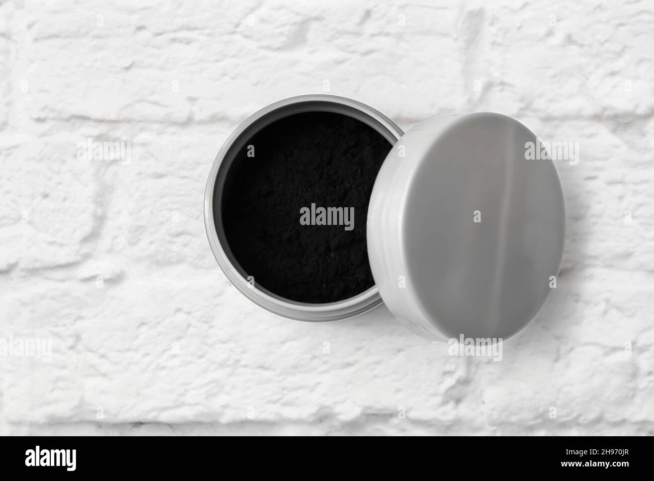 Jar with activated charcoal tooth powder on white brick background ...