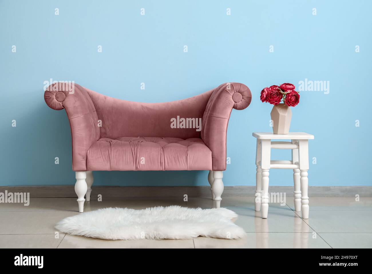 Pink armchair and vase with flowers on stool near blue wall Stock Photo ...