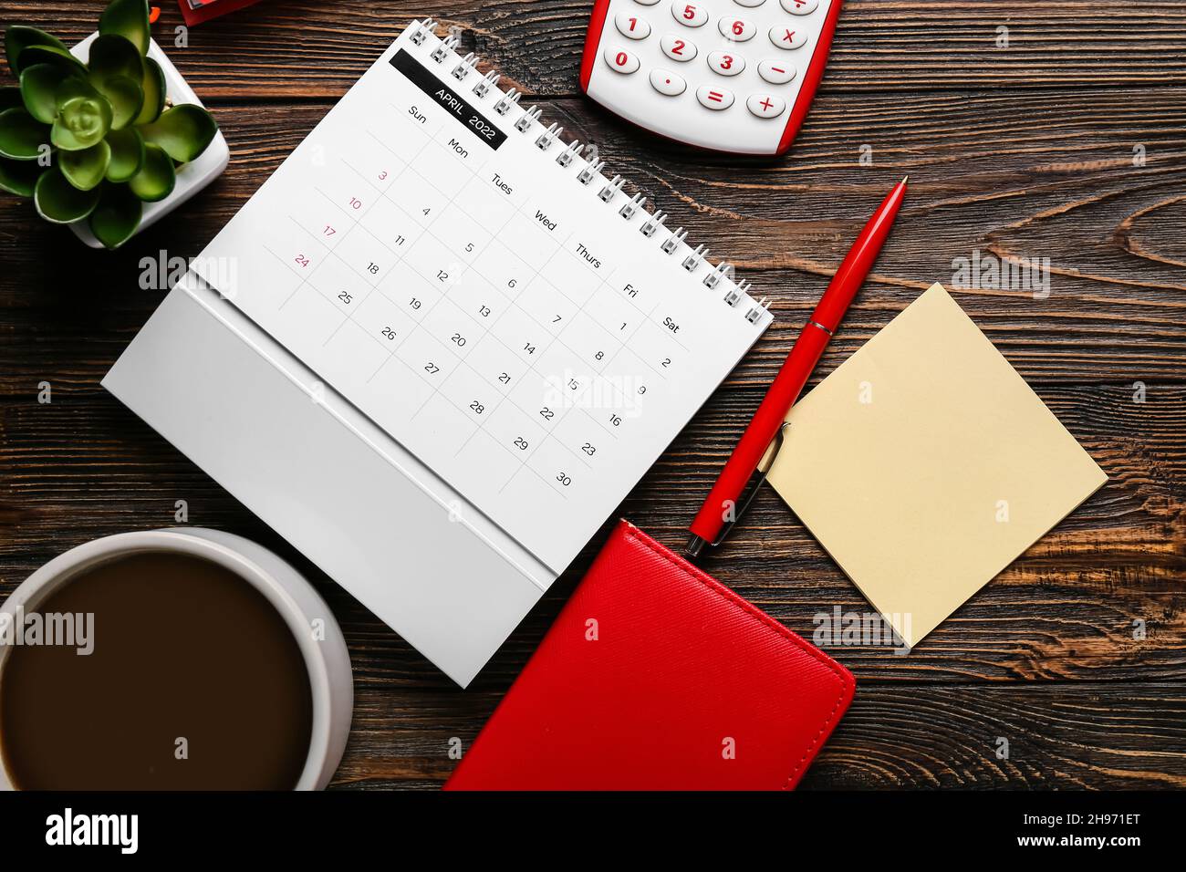 Flip paper calendar for April 2022, sticky notes, notebook, pen and cup ...