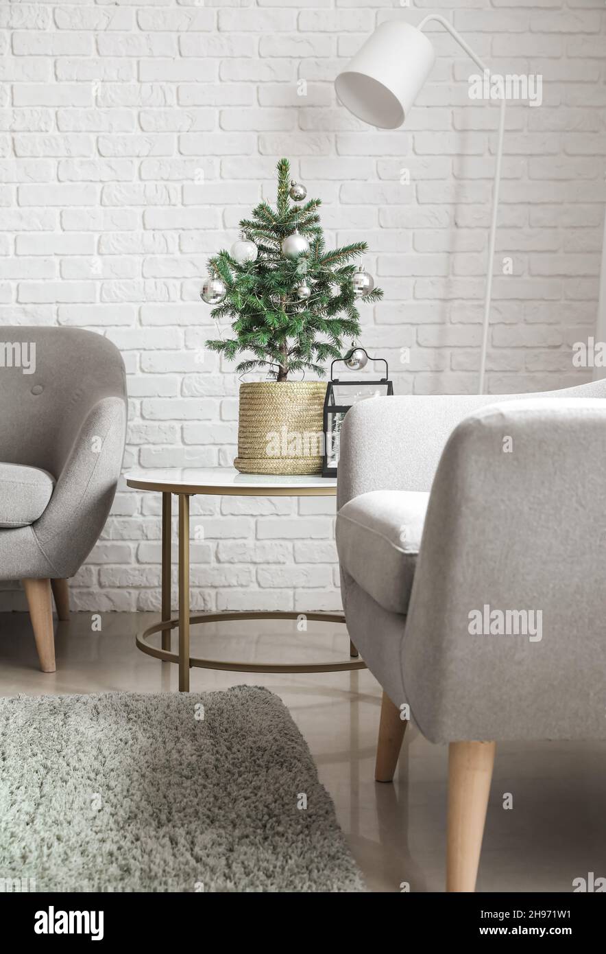 Beautiful Christmas tree on table near white brick wall in living room ...