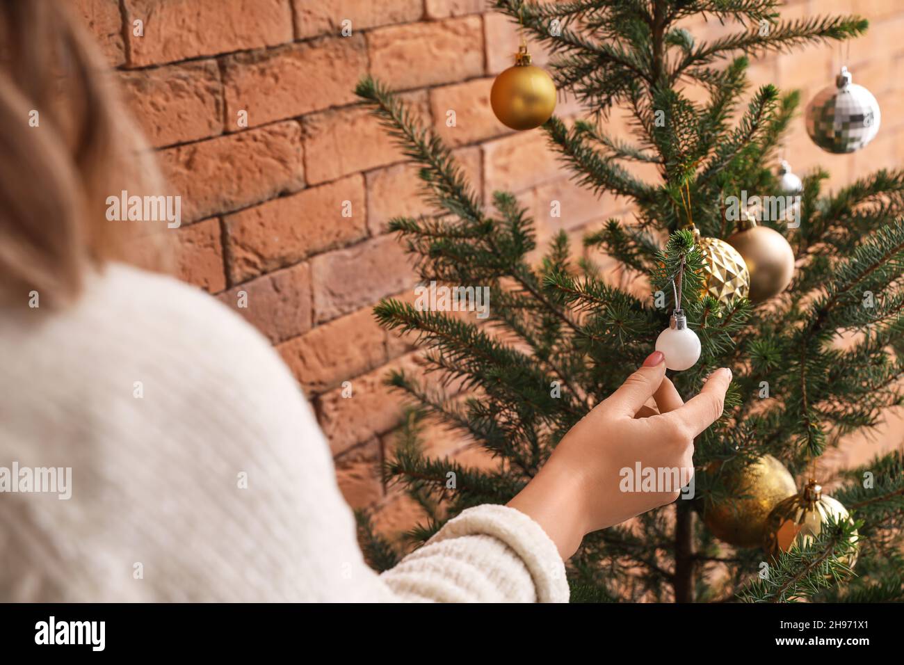 Young woman decorating Christmas tree near brick wall Stock Photo - Alamy