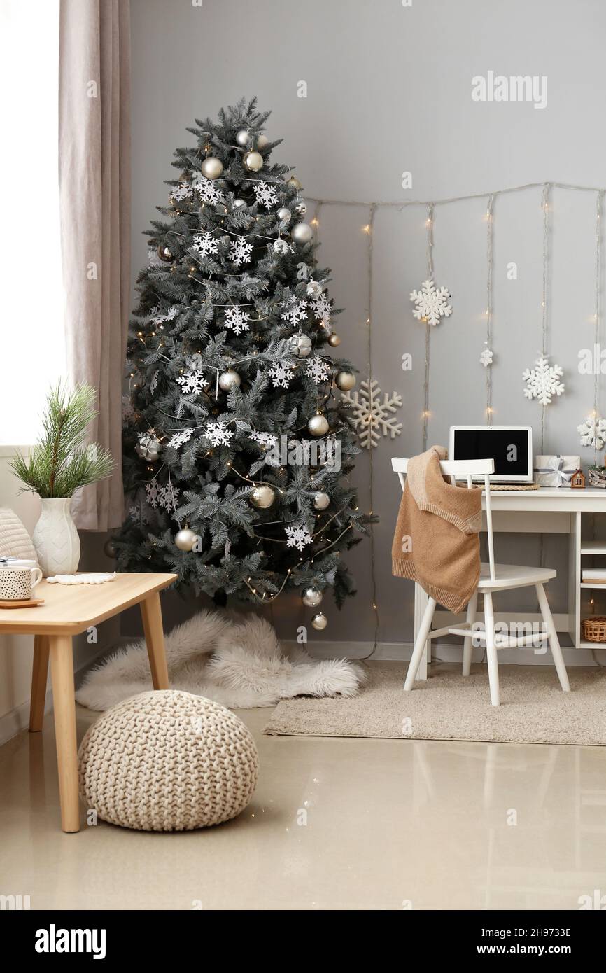 Interior of room with modern workplace and Christmas tree near grey ...