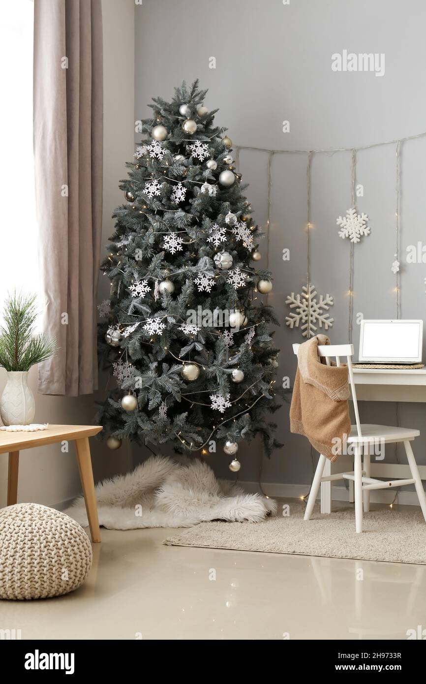 Christmas tree and workplace with modern laptop near grey wall in room ...