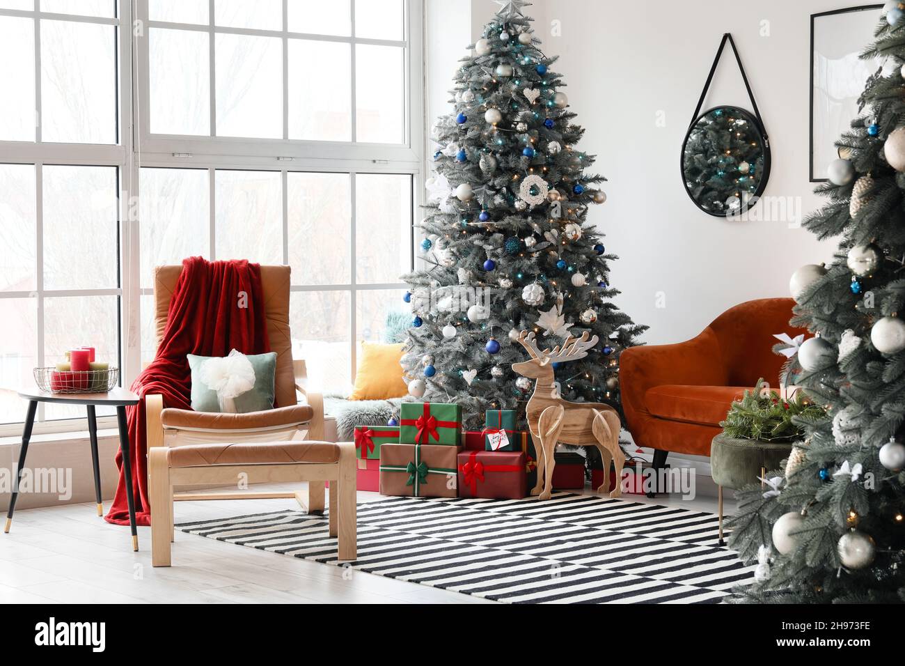 Comfy armchair, Christmas trees with gift boxes and wooden reindeer in ...