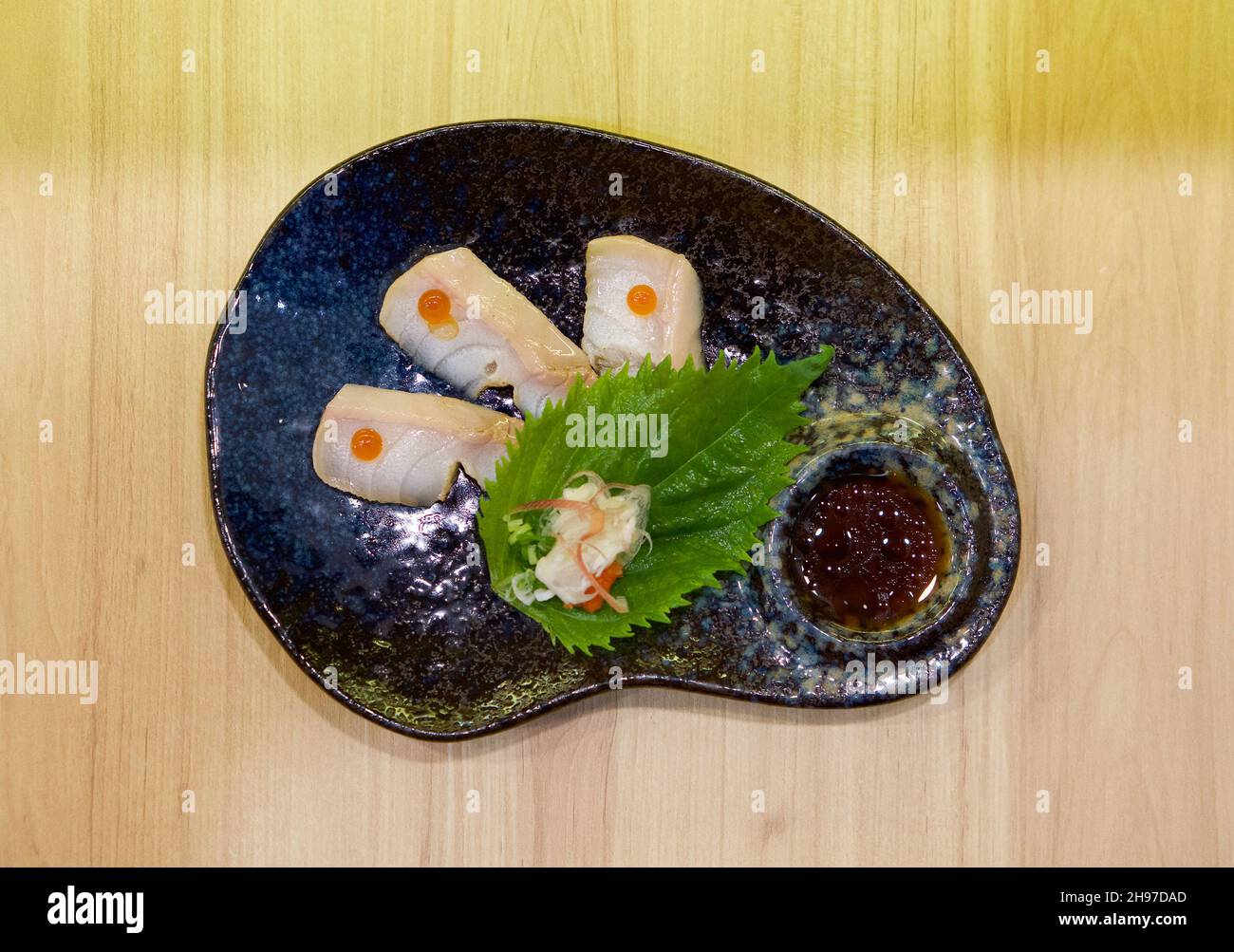 Aburi white fish sliced on top with salmon roe served on dark blue ...