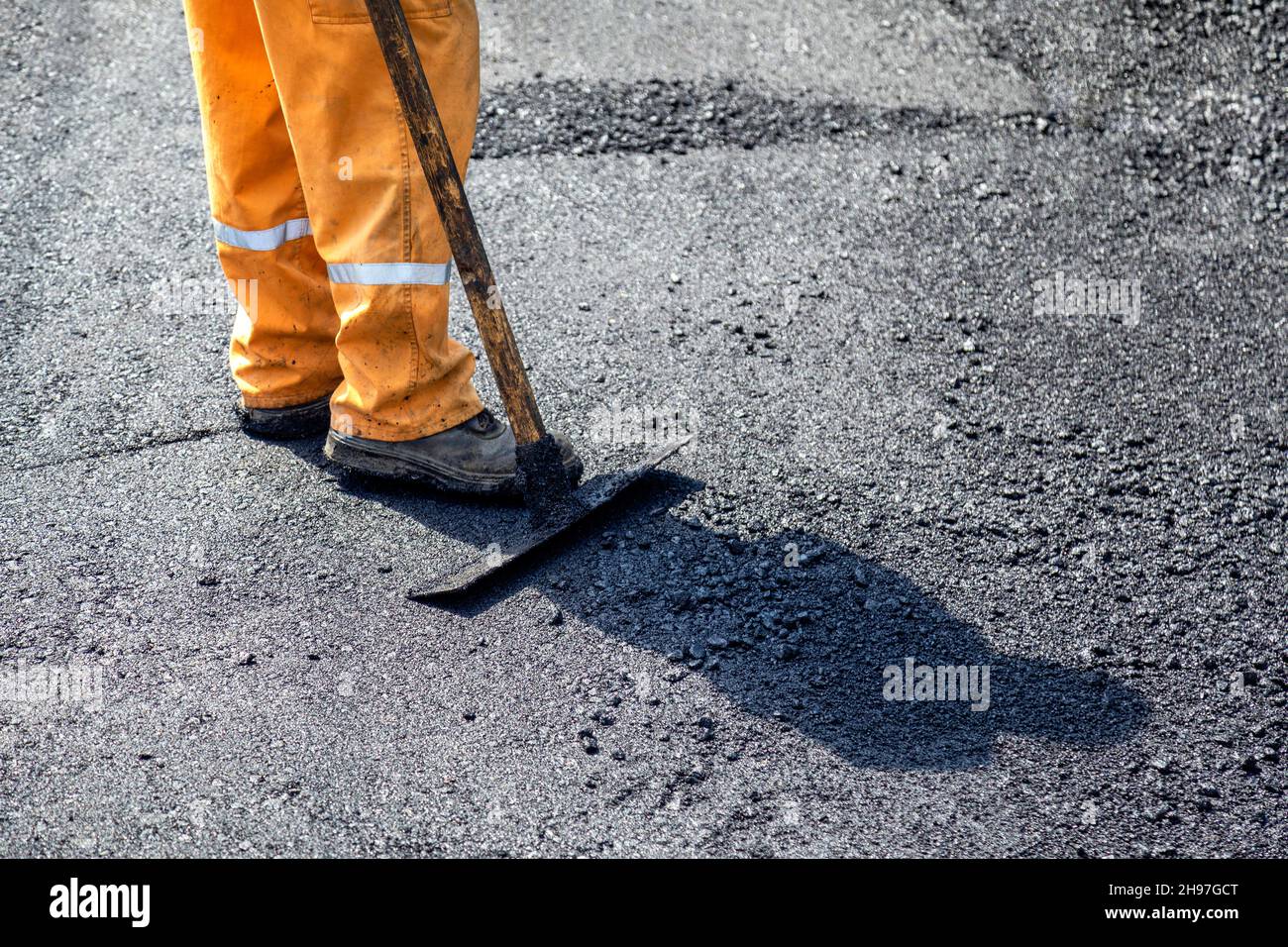 Road construction worker leveling fresh asphalt pavement. Manual labor ...