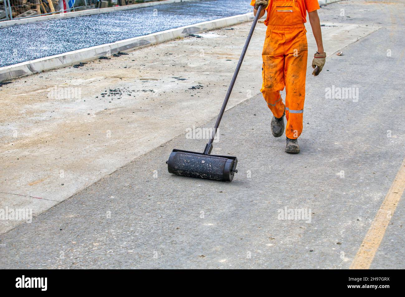 Worker push asphalt wooden hand roller with long handle on road surface ...