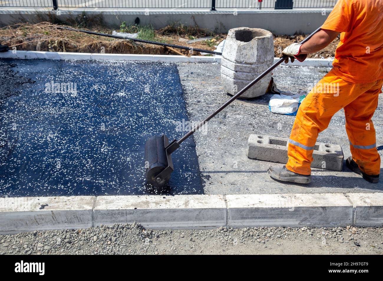 Worker push asphalt wooden hand roller on hot asphalt pavement with ...