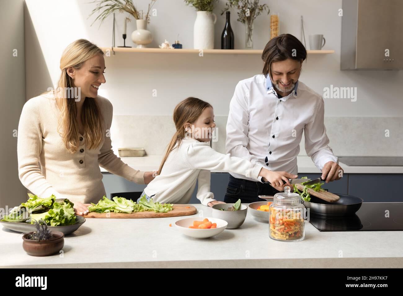 Joyful little girl enjoying cooking with parents at home Stock Photo ...