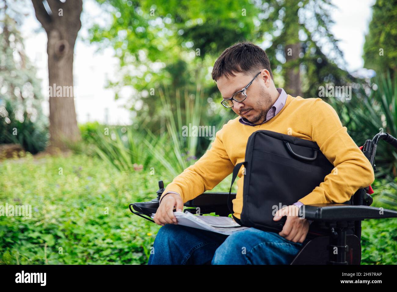 a man with disabilities in a wheelchair works on a laptop remotely ...