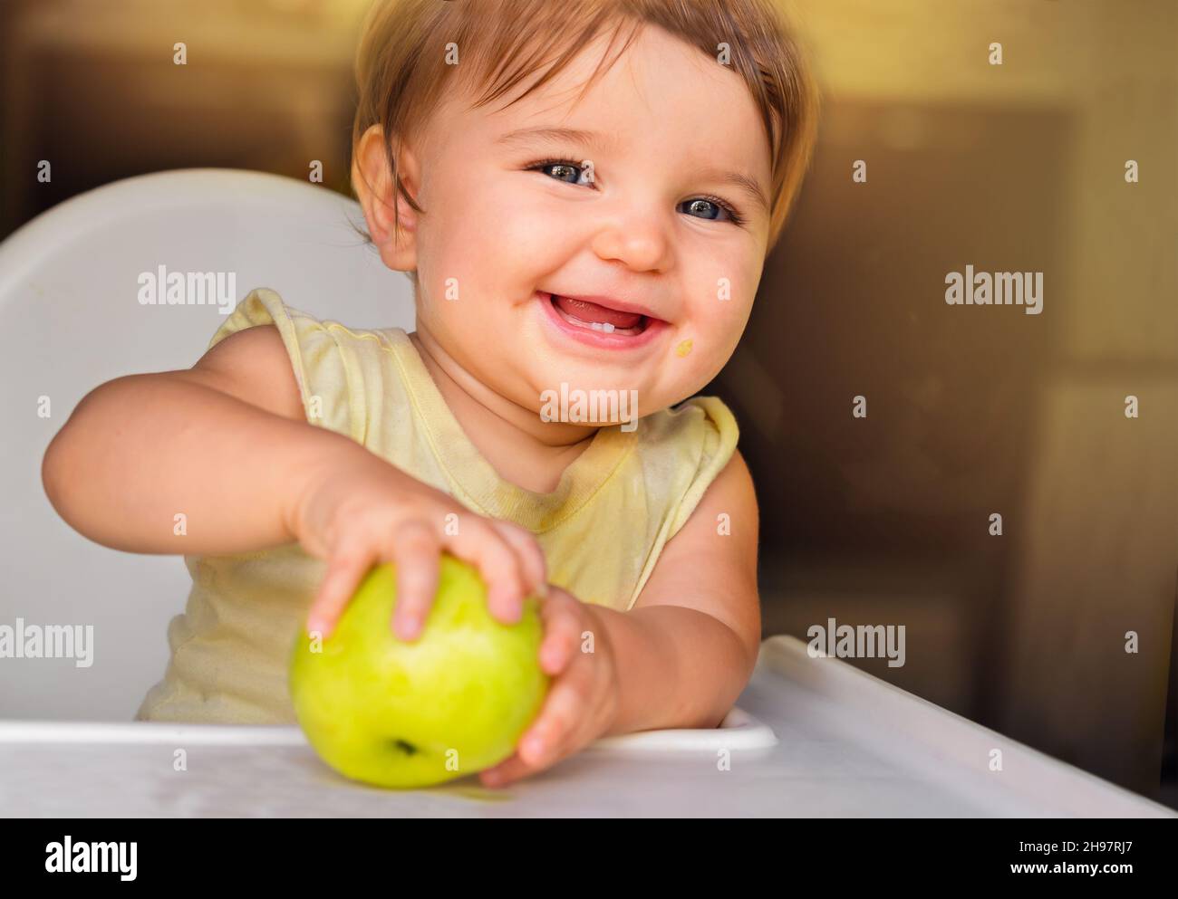 baby with an apple. baby with green apple on baby feeding chair in ...