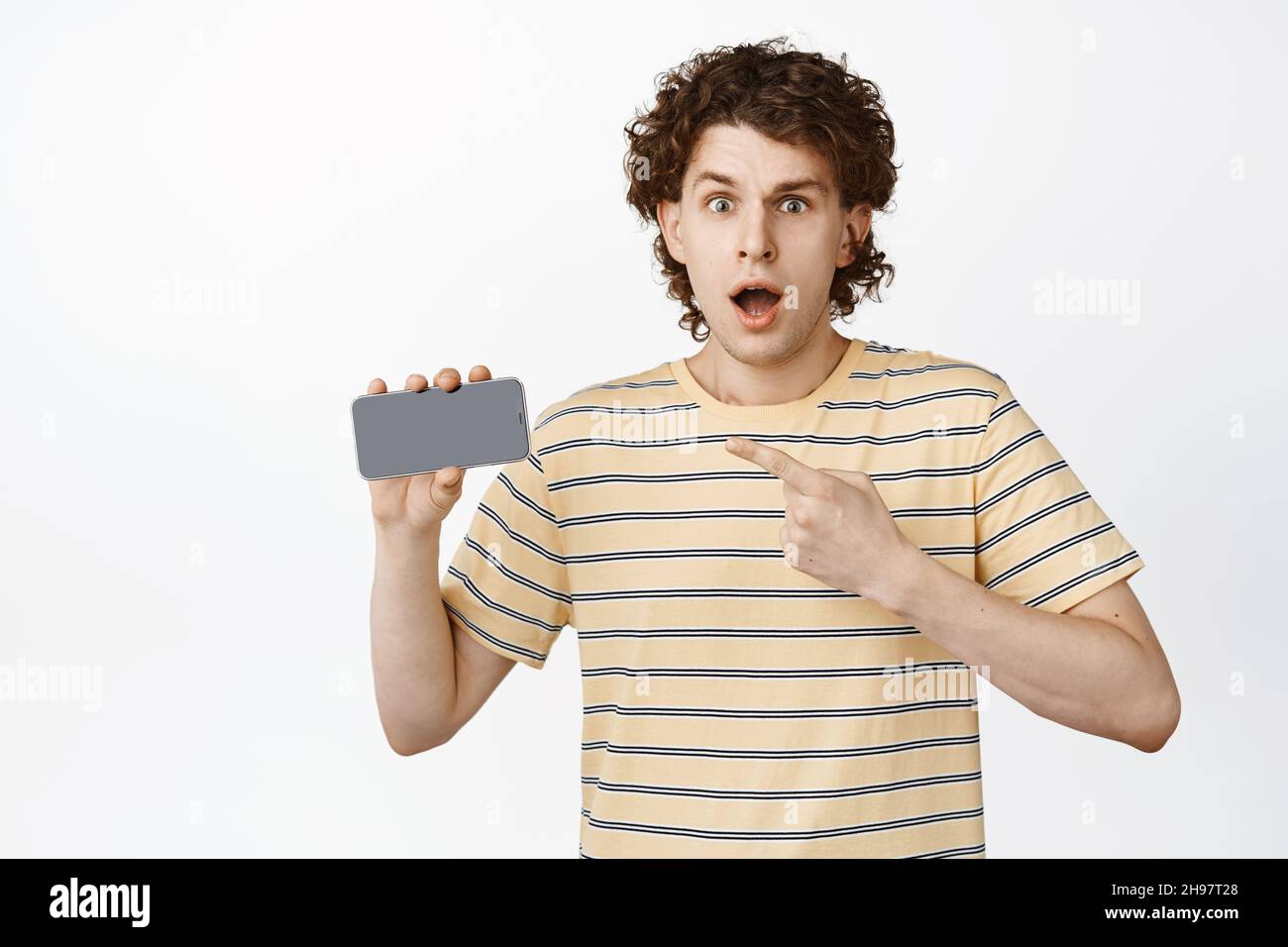 Shocked young man pointing at mobile phone screen, staring amazed at ...