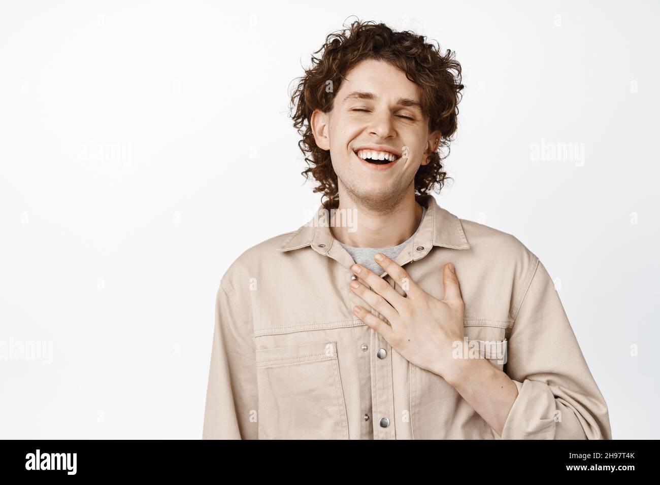 Relieved smiling young man, holding hand on his chest and close eyes ...