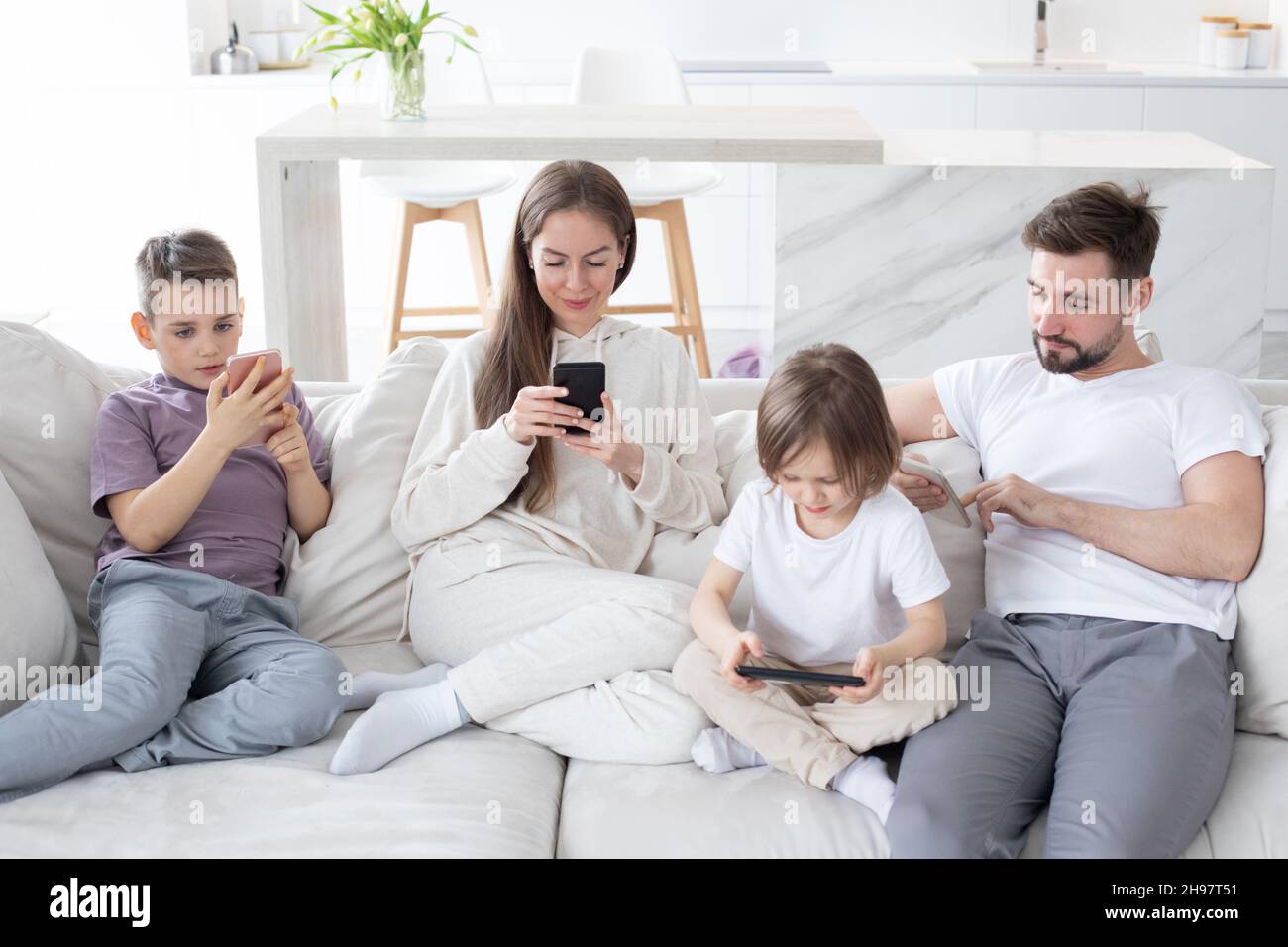 Caucasian parents and kids use devices together sit on sofa, tech ...
