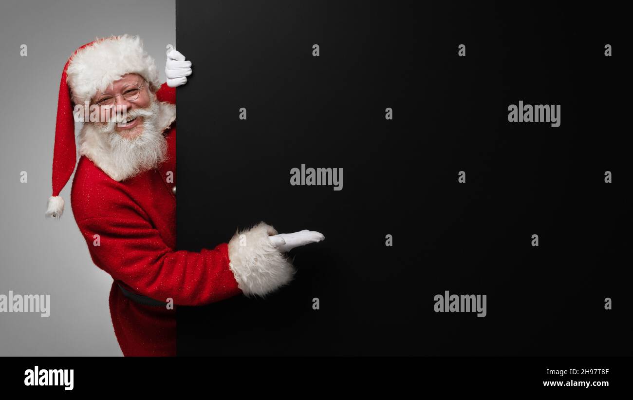 Happy smiling Santa Claus pointing with open hand palm at black banner ...