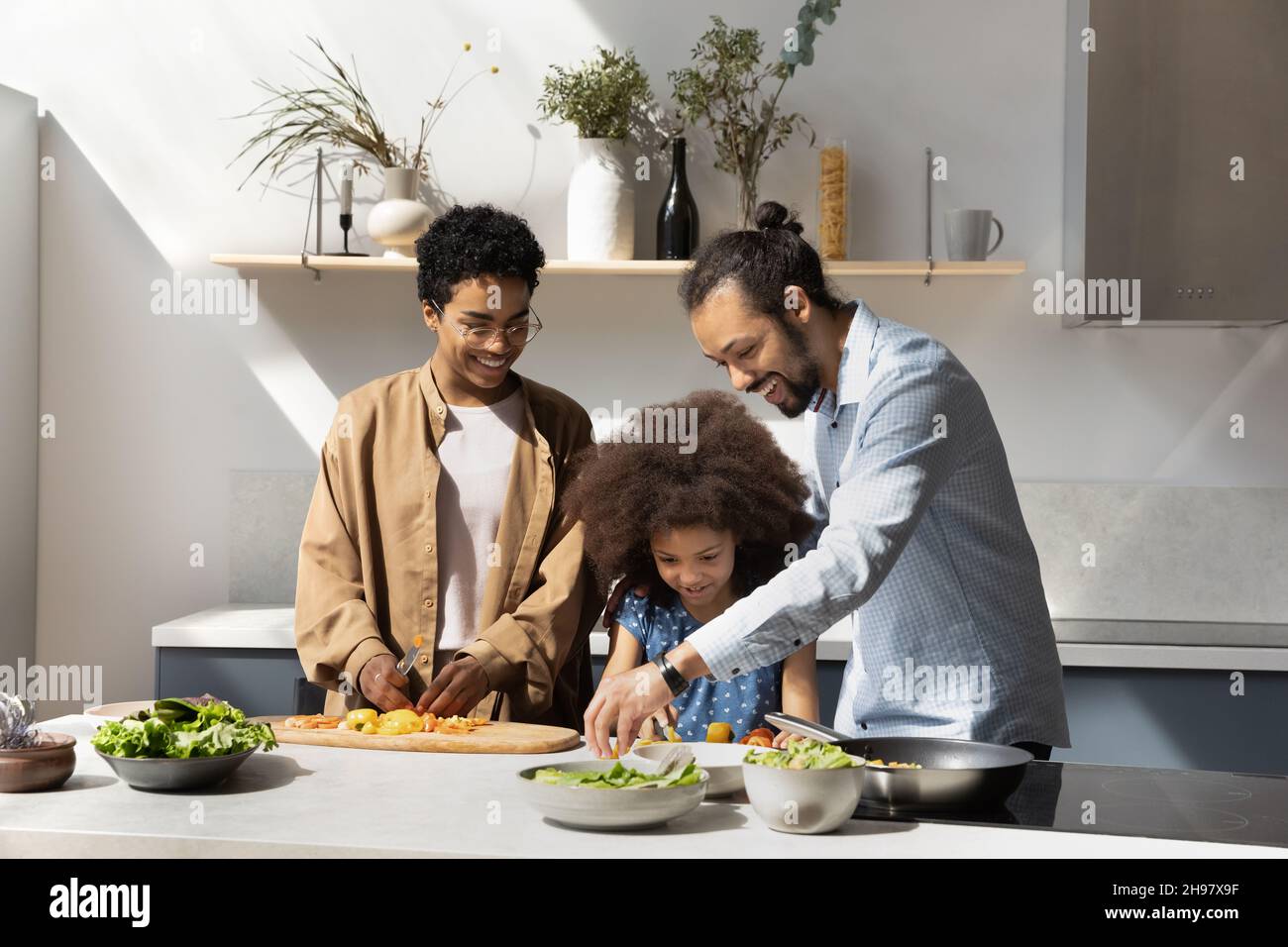 Happy young African American parents teaching little daughter cooking ...