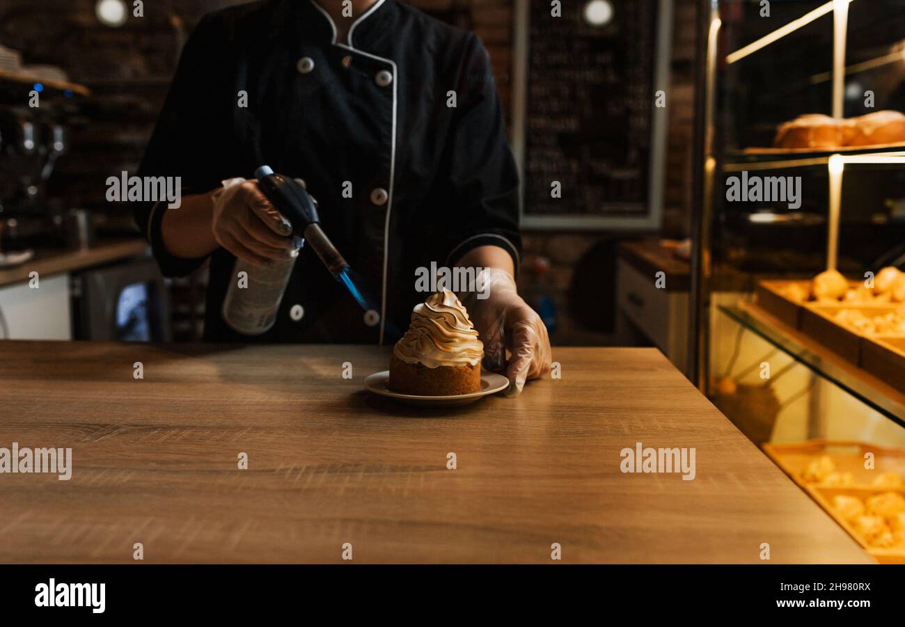 a baker burns protein cream on cakes with a gas burner in the kitchen ...