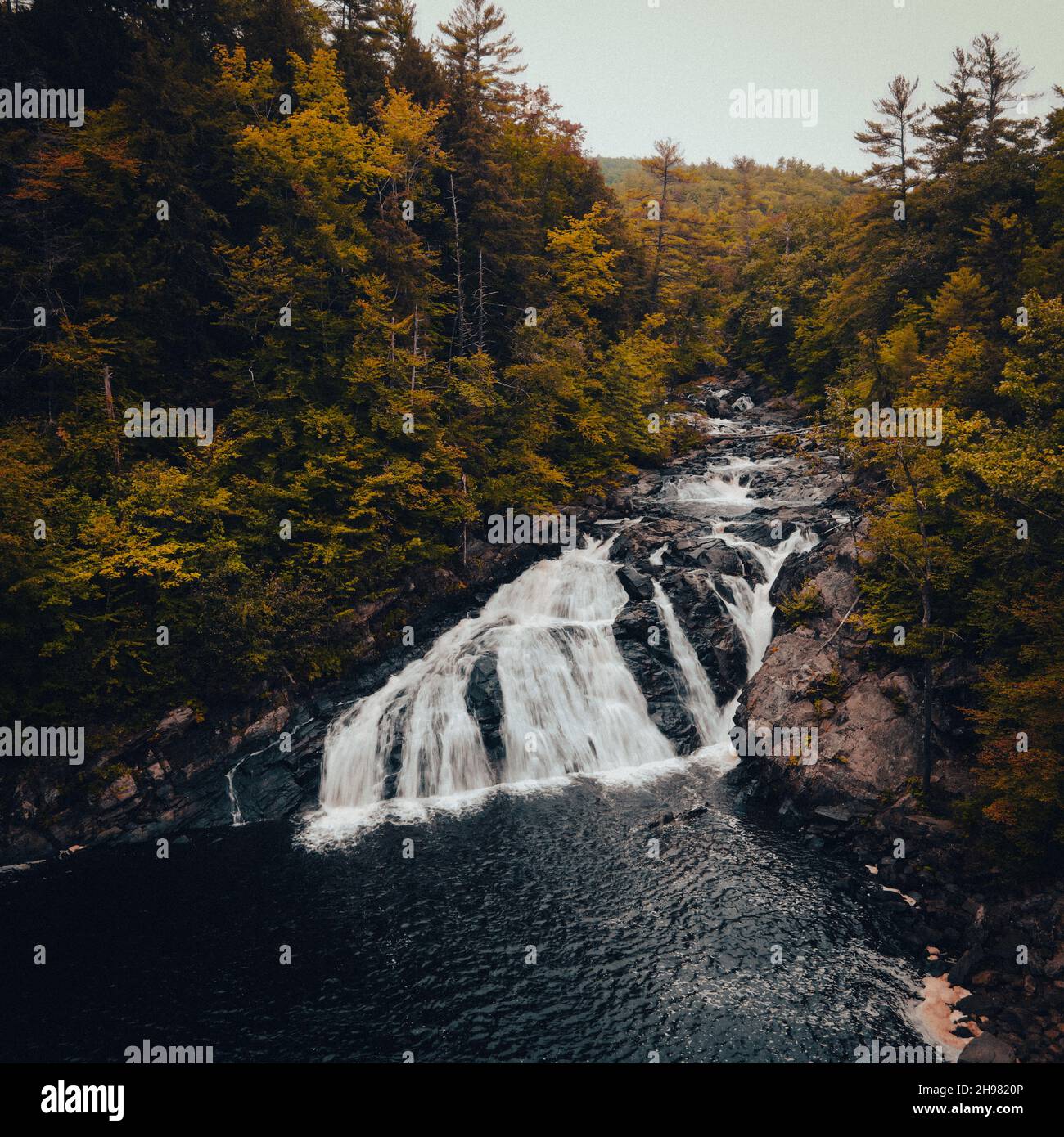 An aerial view of a beautiful waterfall going throught the forests ...