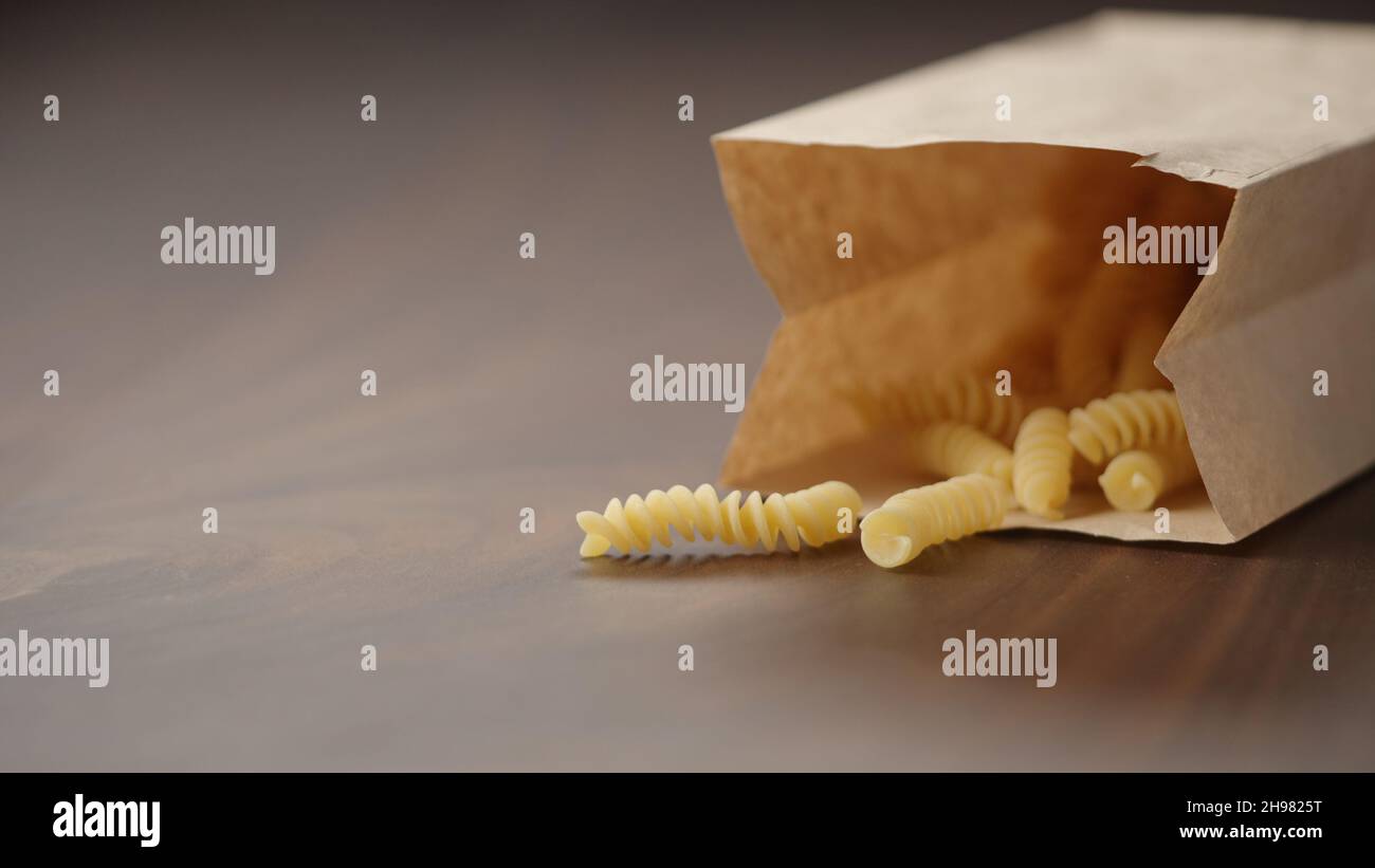 dry organic bronze cut fusilli spill out from paper bag on walnut table ...