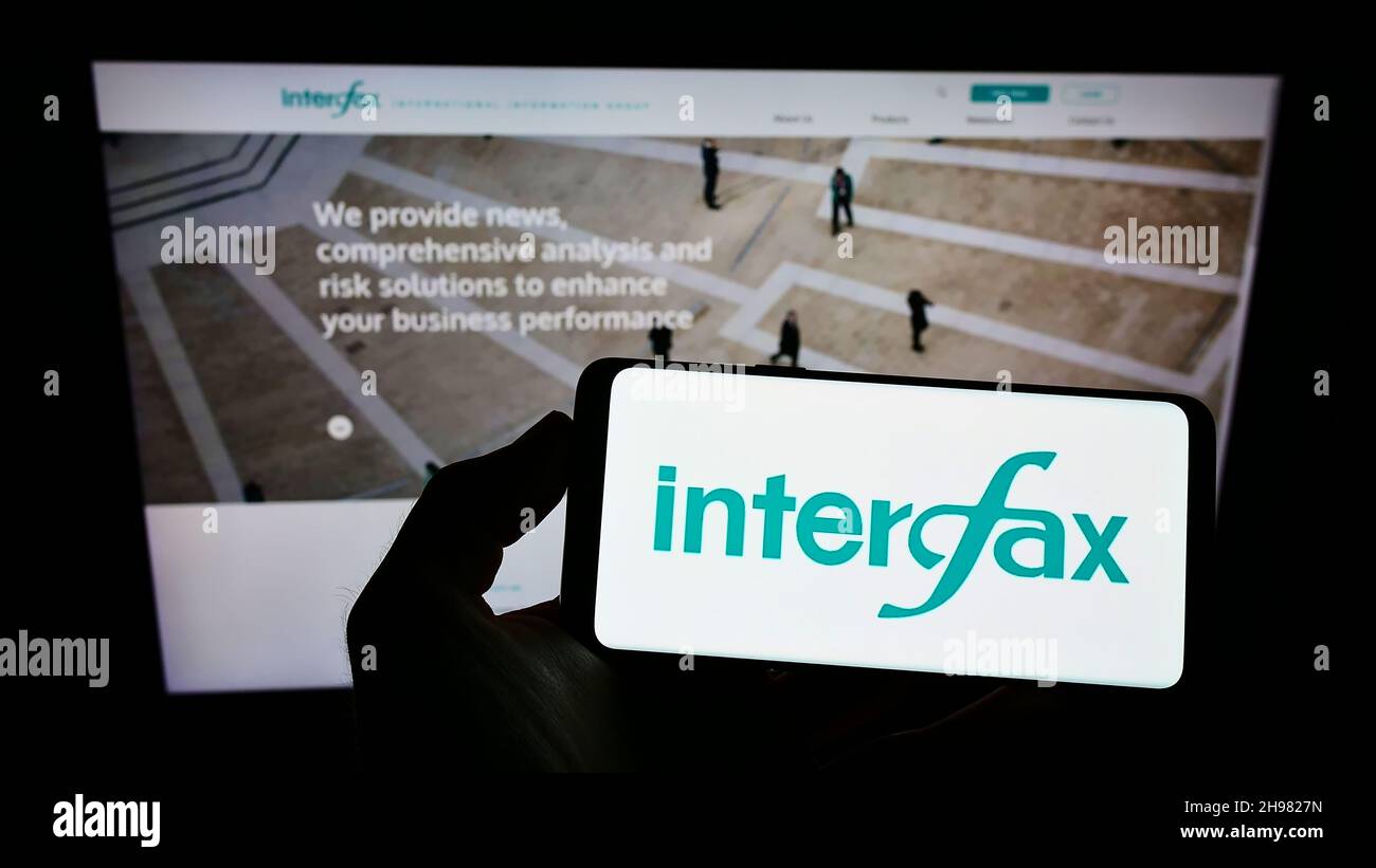 Person holding mobile phone with logo of Russian news agency Interfax ...