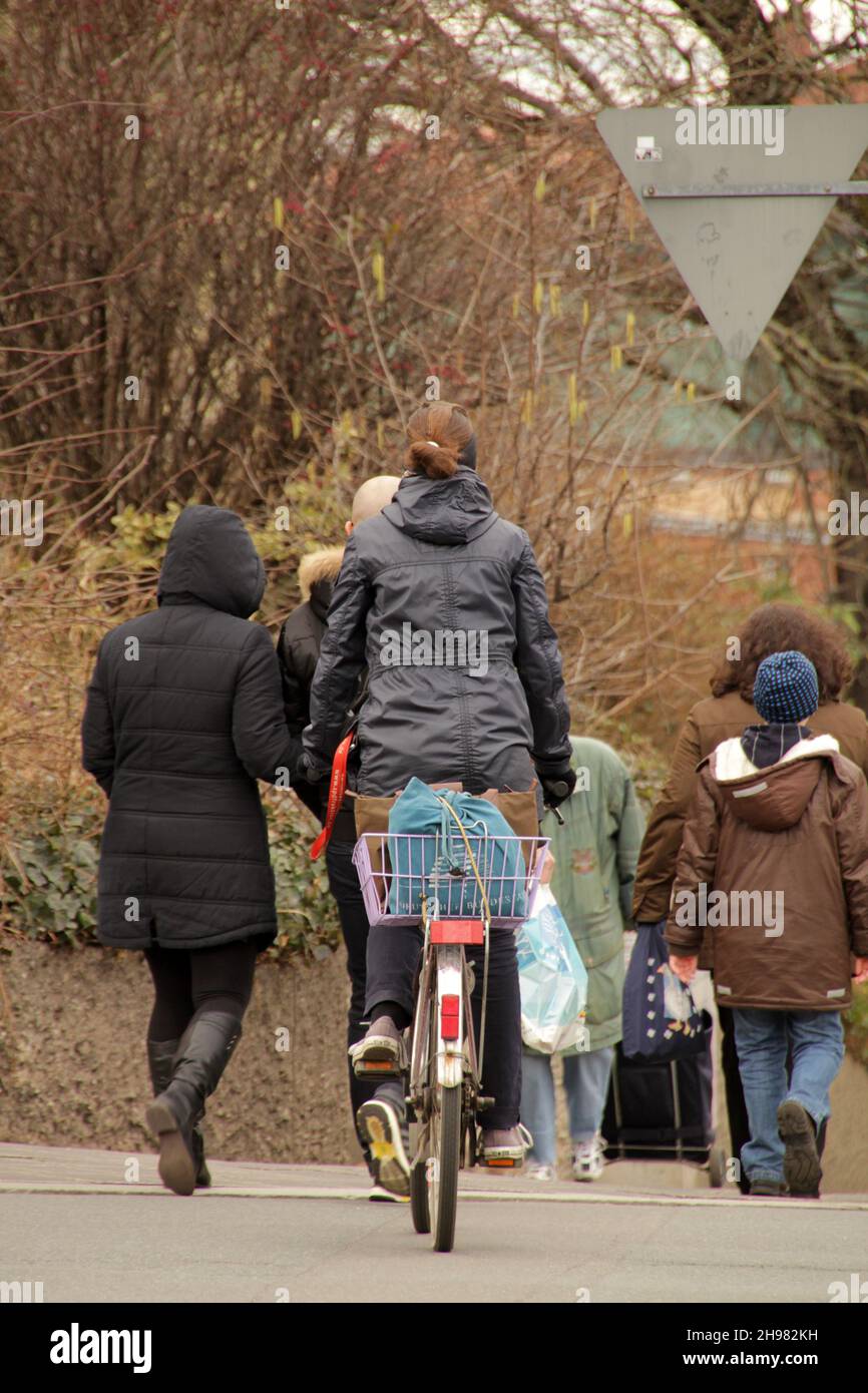 A vertical back view of people walking and riding bikes in a park in ...