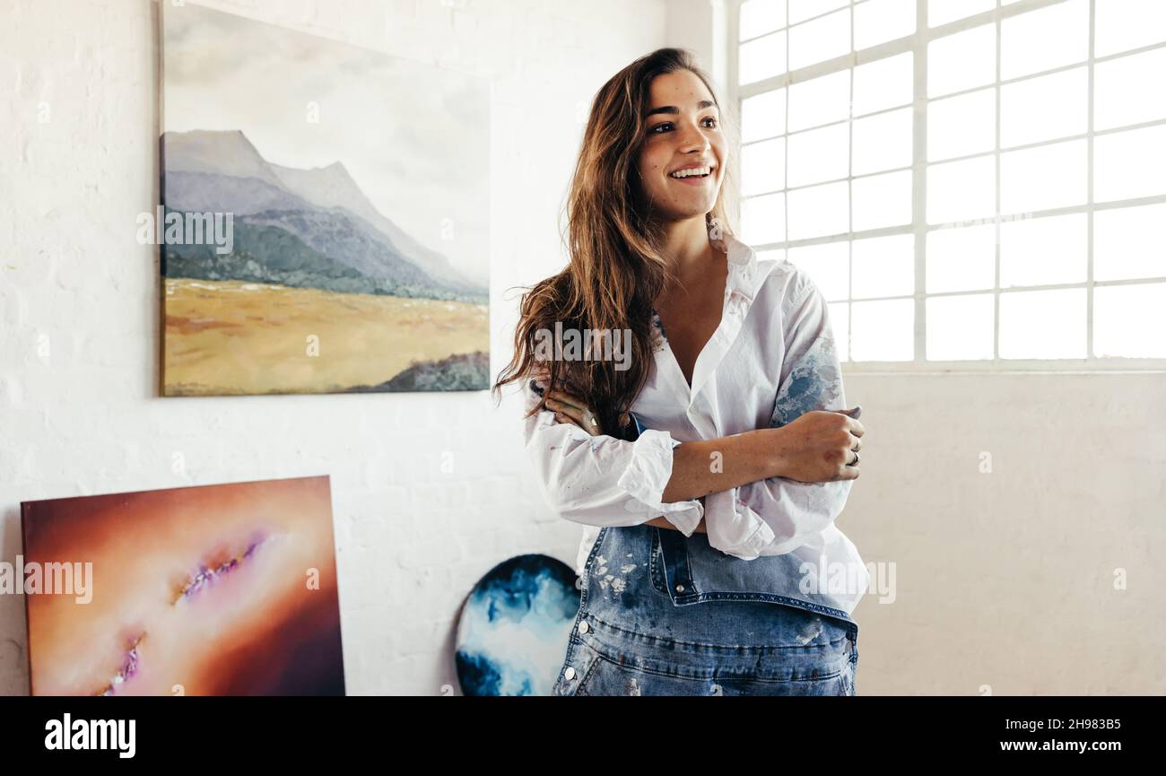 Thoughtful female artist standing in front of her paintings. Female ...