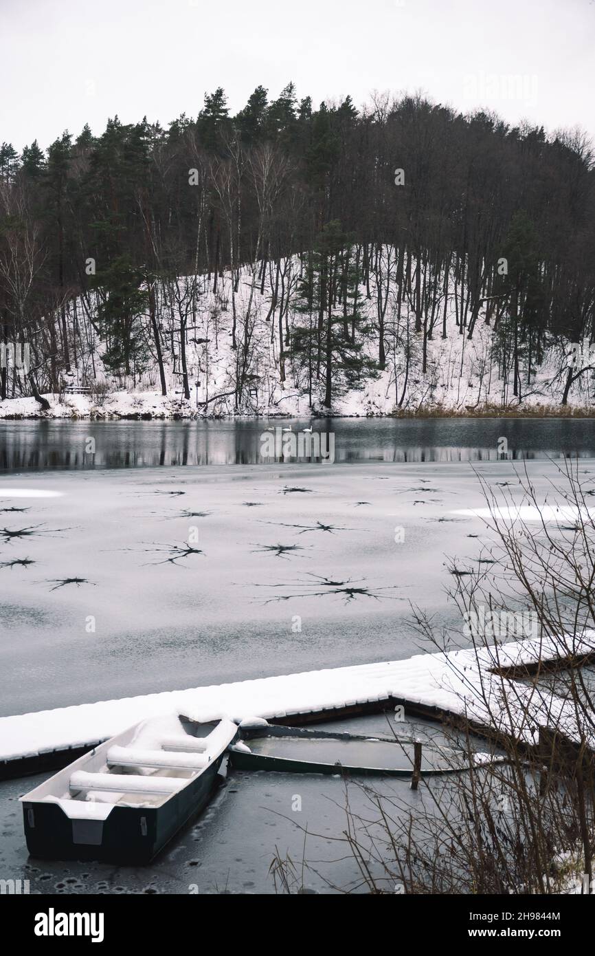 Freezing lake in winter with holes, with pier, wooden boats and fir ...