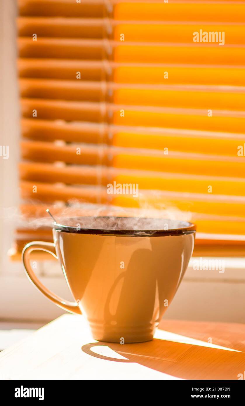 Morning cup of coffee on a window sill. Steam above the ceramics cup ...