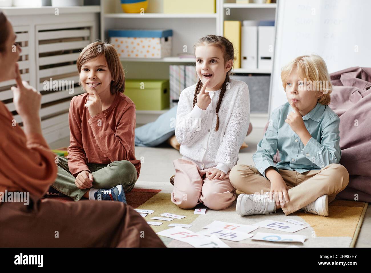 A group of children sitting on the floor and repeating new words after ...