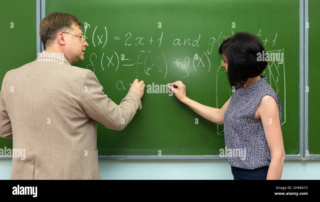 An adult teacher at the blackboard explains the solution of a math ...