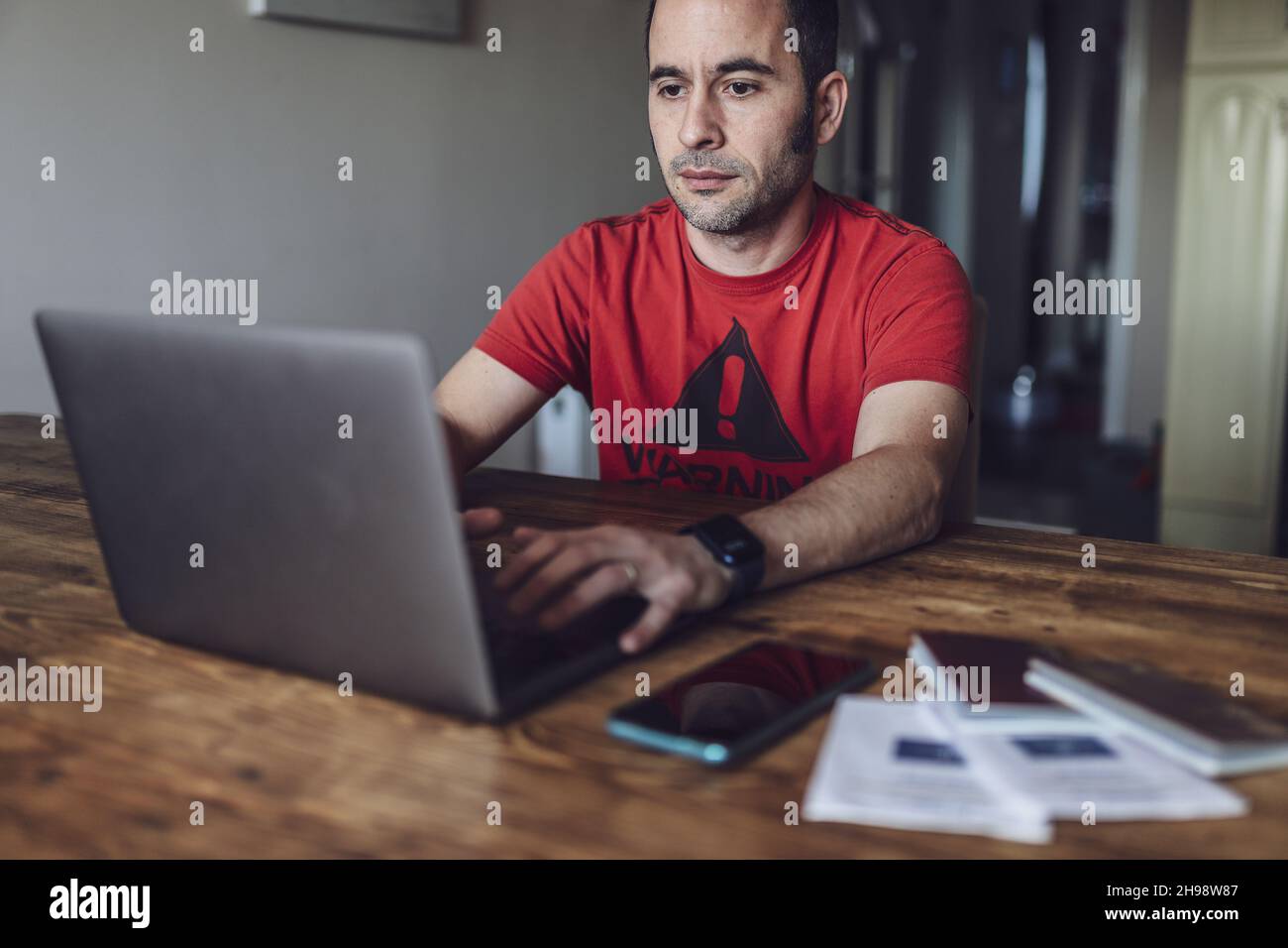 A white man using a laptop on a wooden table with a cellphone ...