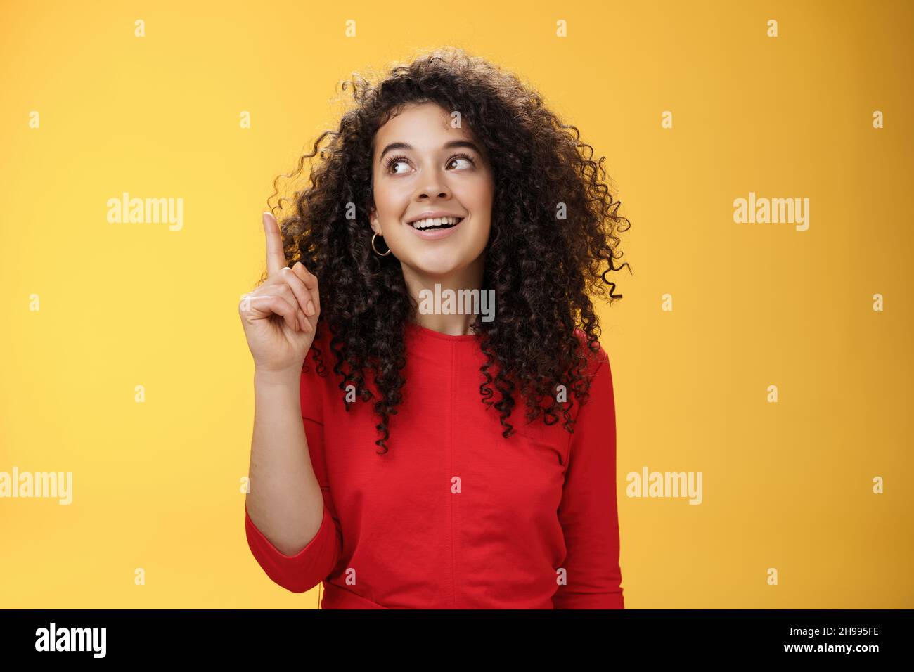 I got idea. Excited happy attractive woman with curly hair in red dress raising index finger in ...