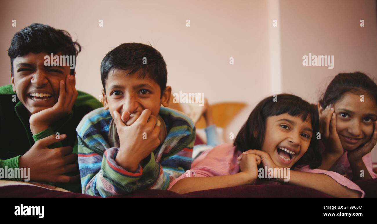 A shallow focus of four siblings enjoying a funny show on the ...