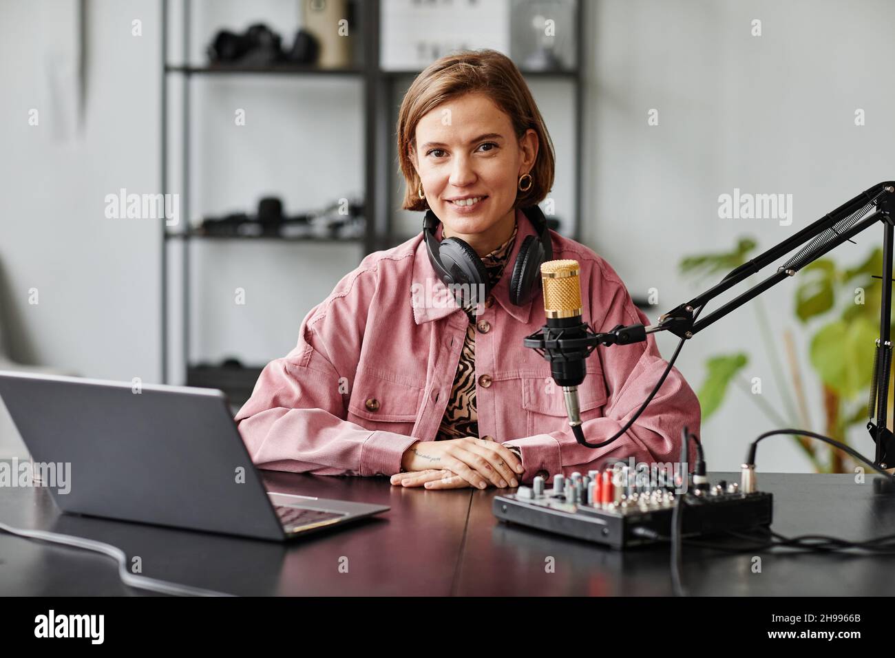 Portrait of young female creator smiling at camera in recording studio ...