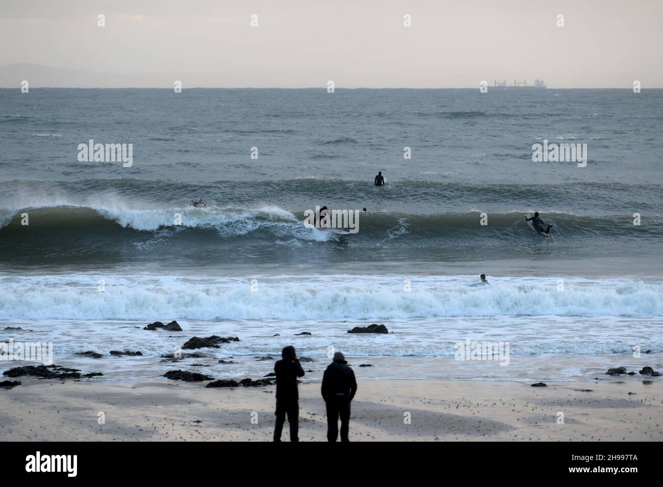 Surfing in Wales. Al ongboarder races thebreaking wave at Langland Bay ...