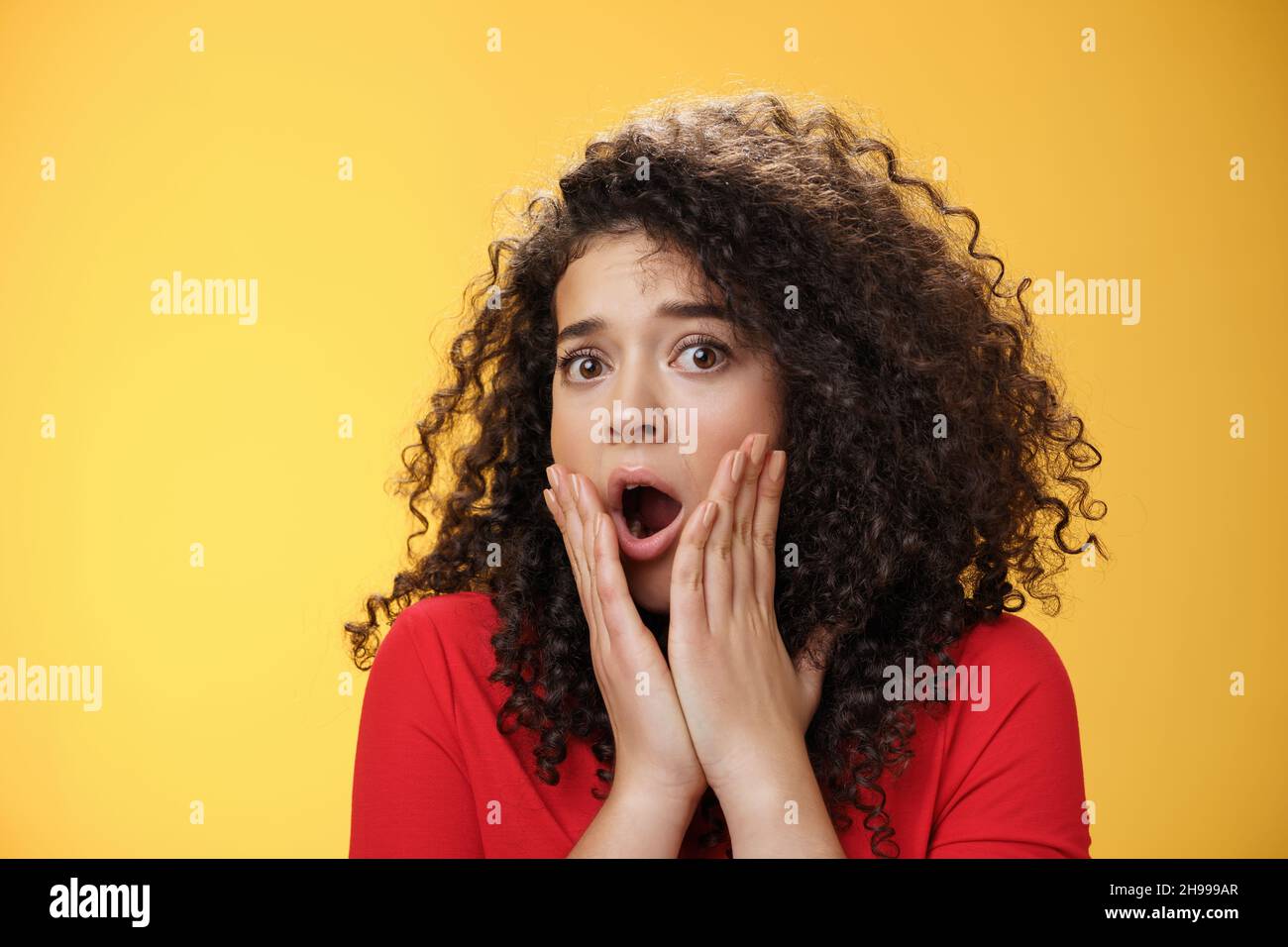 Indoor shot of shocked female drama queen with curly hair gasping in ...