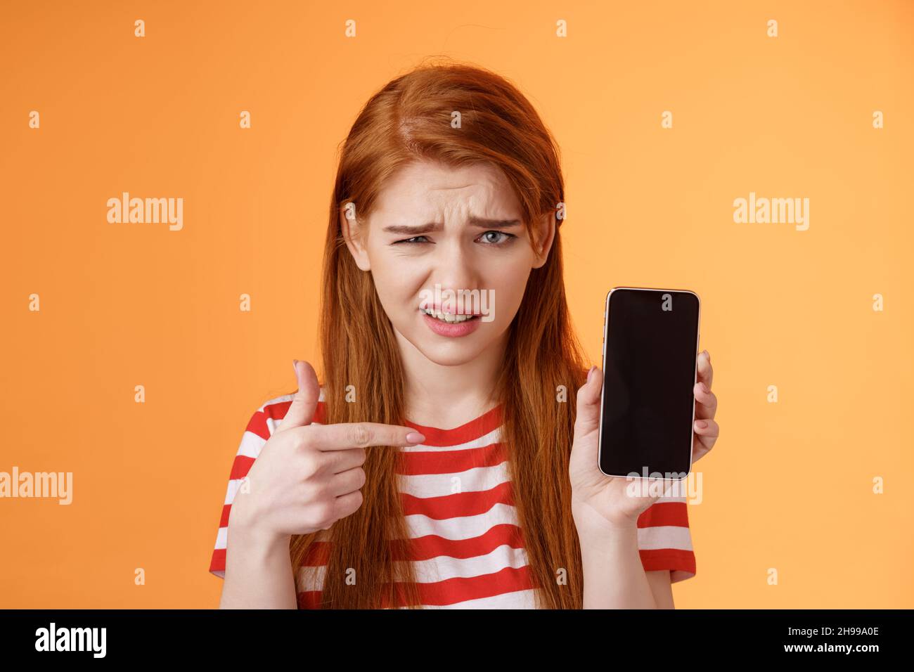 Perplexed disappointed redhead girl show smartphone screen app ...