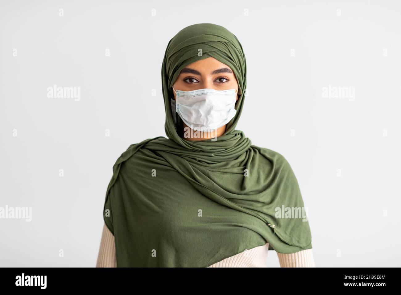 Pretty millennial Arab female in hijab wearing medical mask during ...