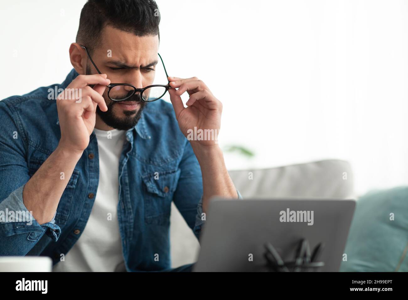 Frustrated young Arab man touching glasses, looking at laptop screen ...