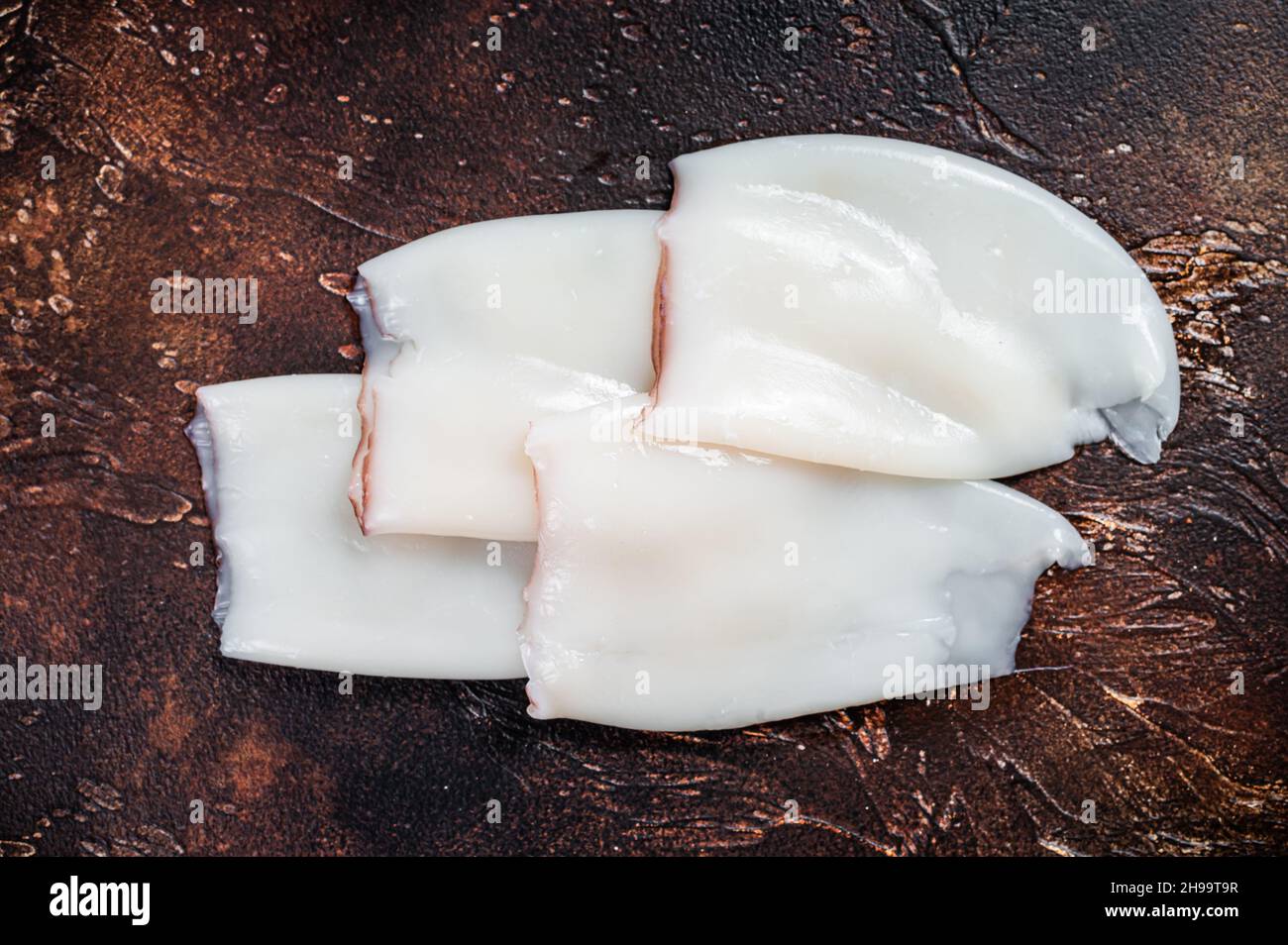 Raw Squid or Calamari tubes on a kitchen table. Dark background. Top ...