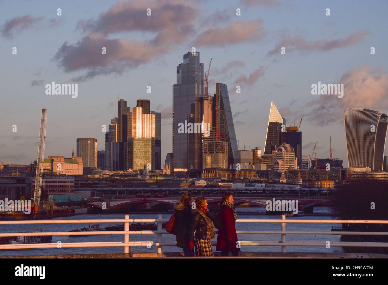 People walk in Waterloo Bridge past the City of London skyline, the ...