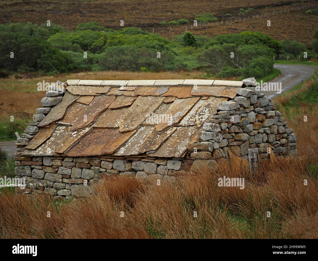 small bothy with stone walls and vernacular flagstone roof by roadside ...