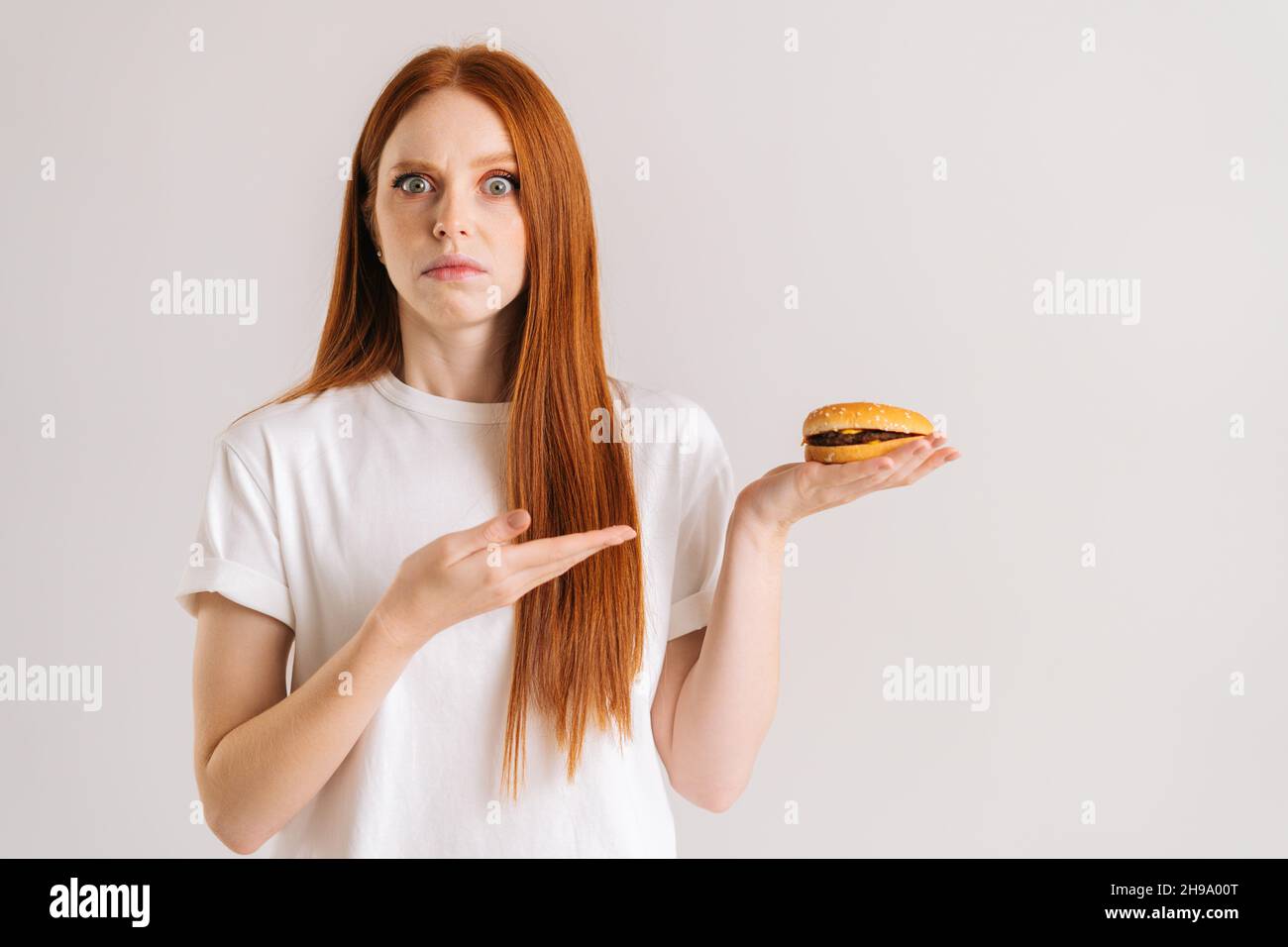Studio portrait of shocked pretty young woman pointing to tasty burger ...