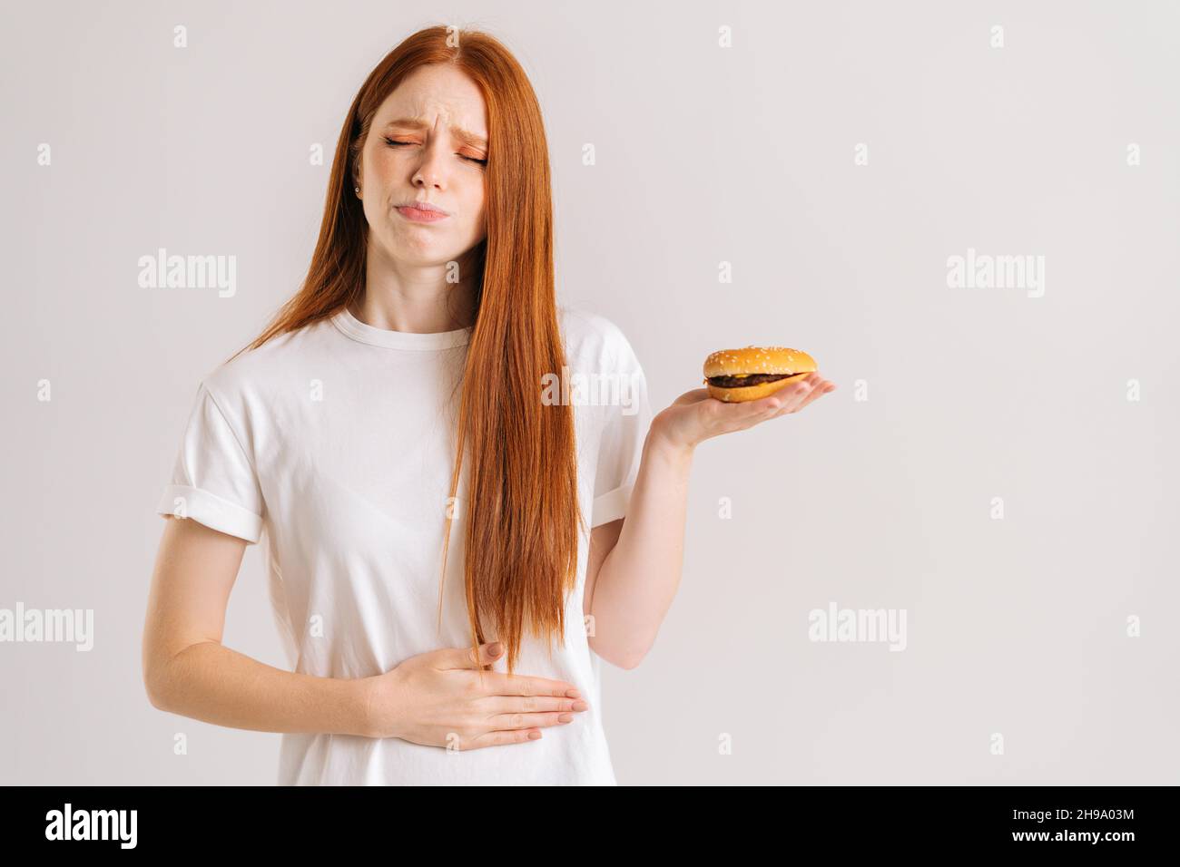 Studio portrait of hungry young woman with disgust holding burger ...